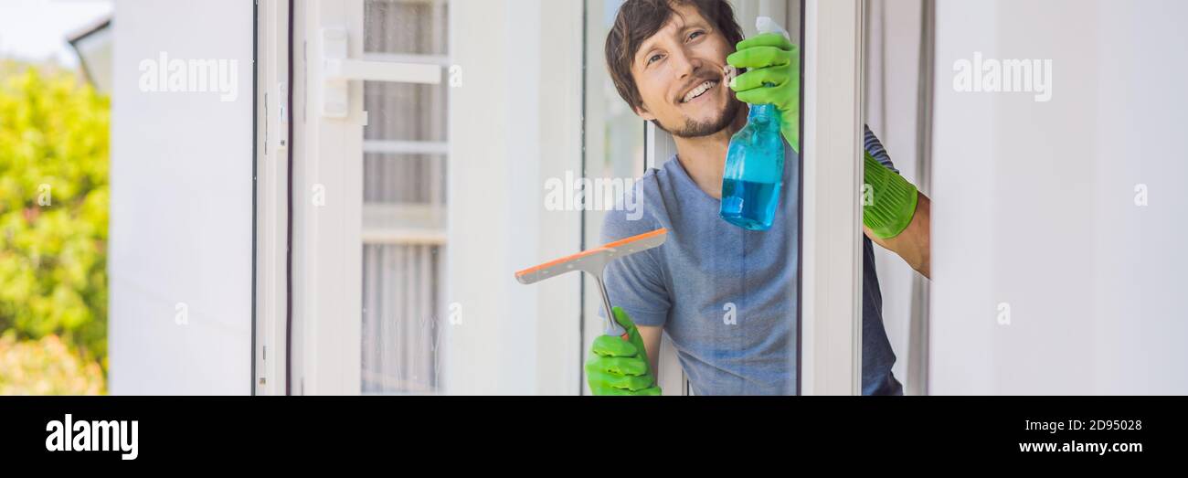 A young man cleaning the window with a window cleaner BANNER, LONG ...