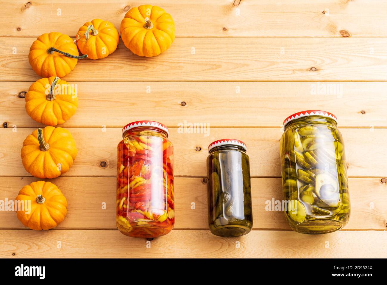 Jars with pickled cucumbers and pepper and pumpkins on wooden surface ...