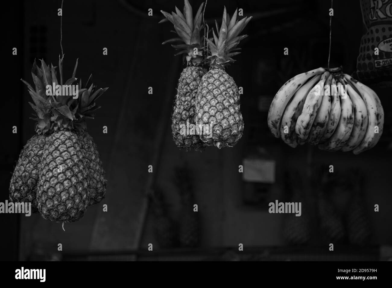Grayscale shot of pineapples and bananas hanging on ceiling Stock Photo ...