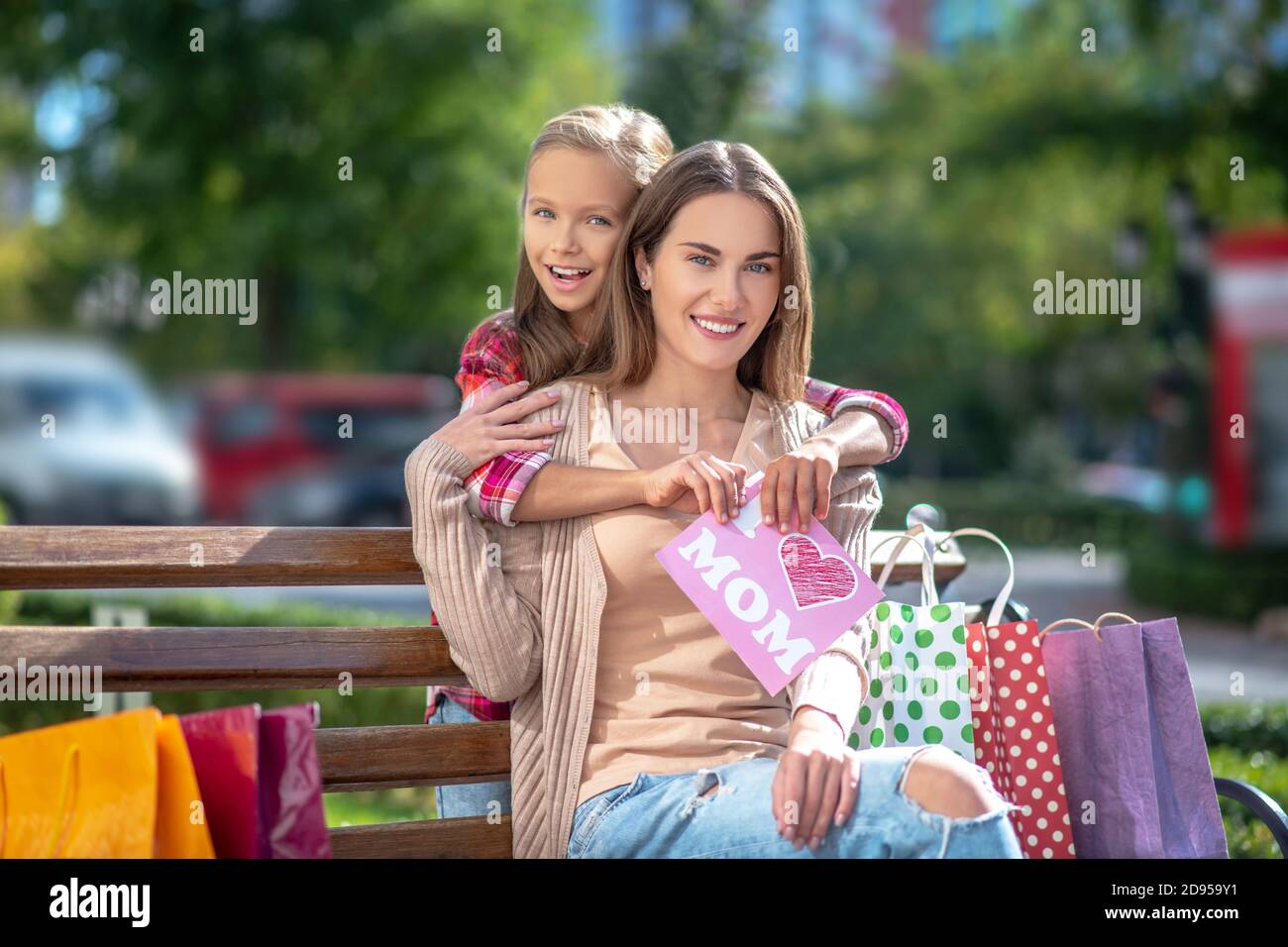 Happy daughter hugging her mom sitting on park bench Stock Photo - Alamy