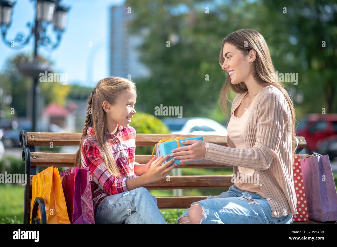 Smiling mom giving her daughter present on park bench Stock Photo - Alamy