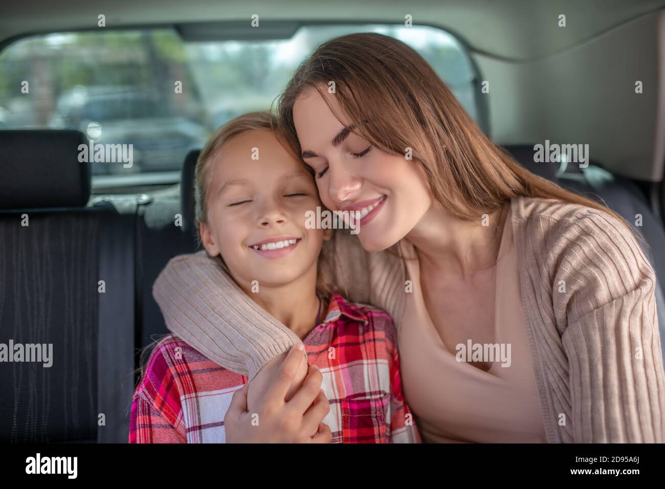 Mom embracing her daughter, sitting cheek to cheek on backseat of car ...