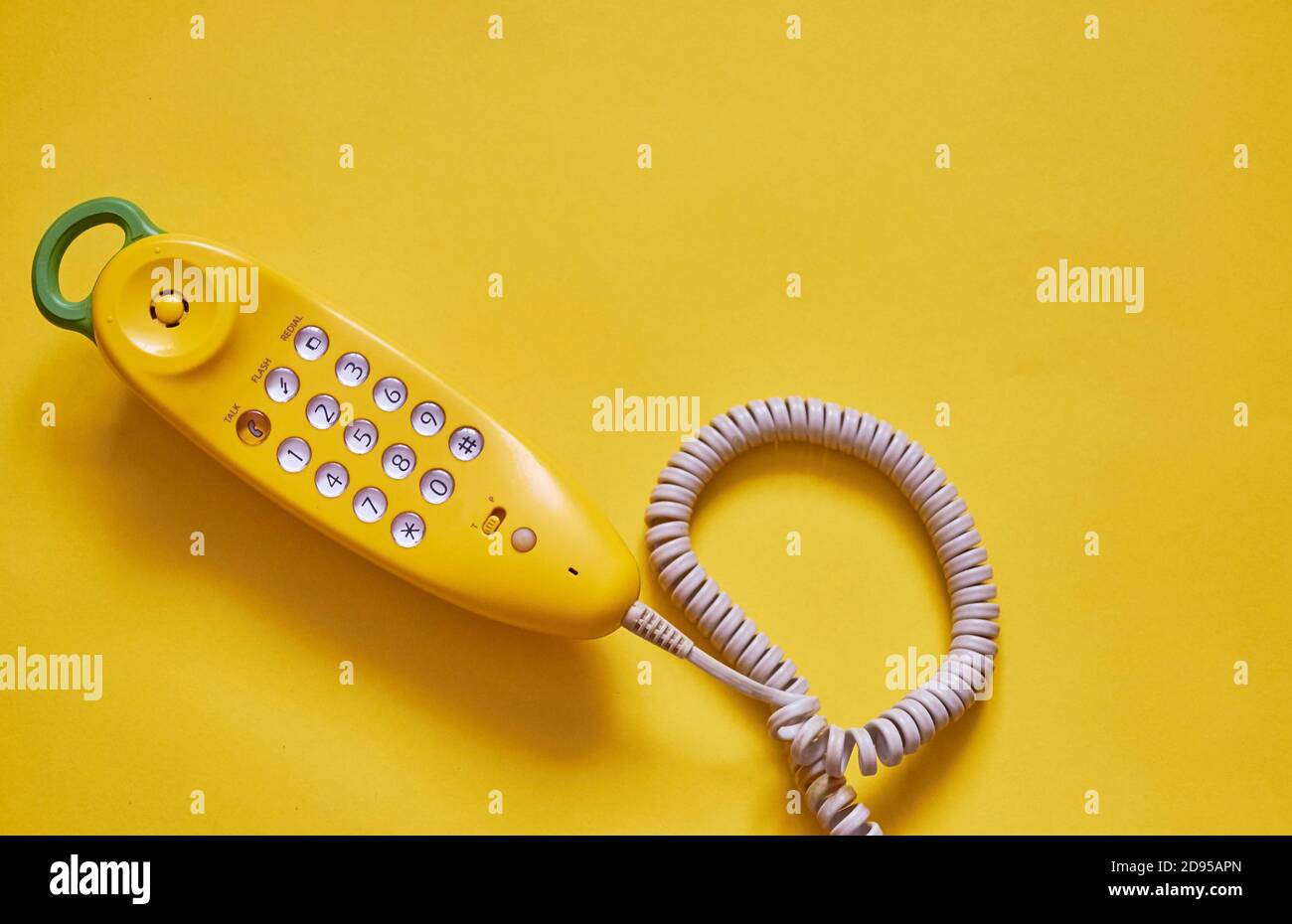 A yellow telephone receiver with a wire lies on a yellow background ...