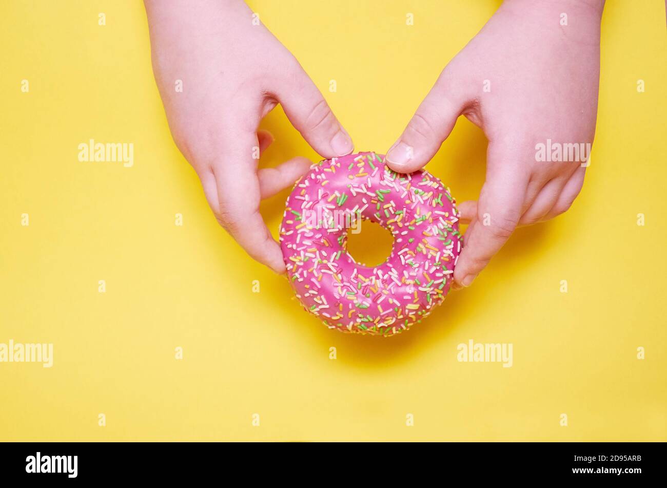 Two hands hold a pink donut. The view from the top. Yellow background ...