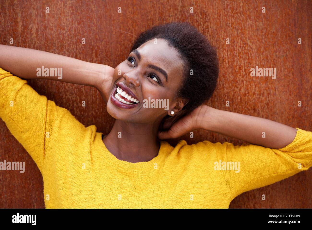Close up portrait of happy young black woman smiling with hands behind ...