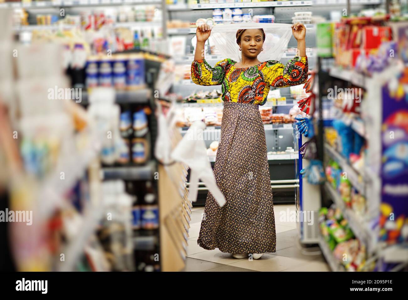 Happy african woman in traditional clothes and veil looking product at ...