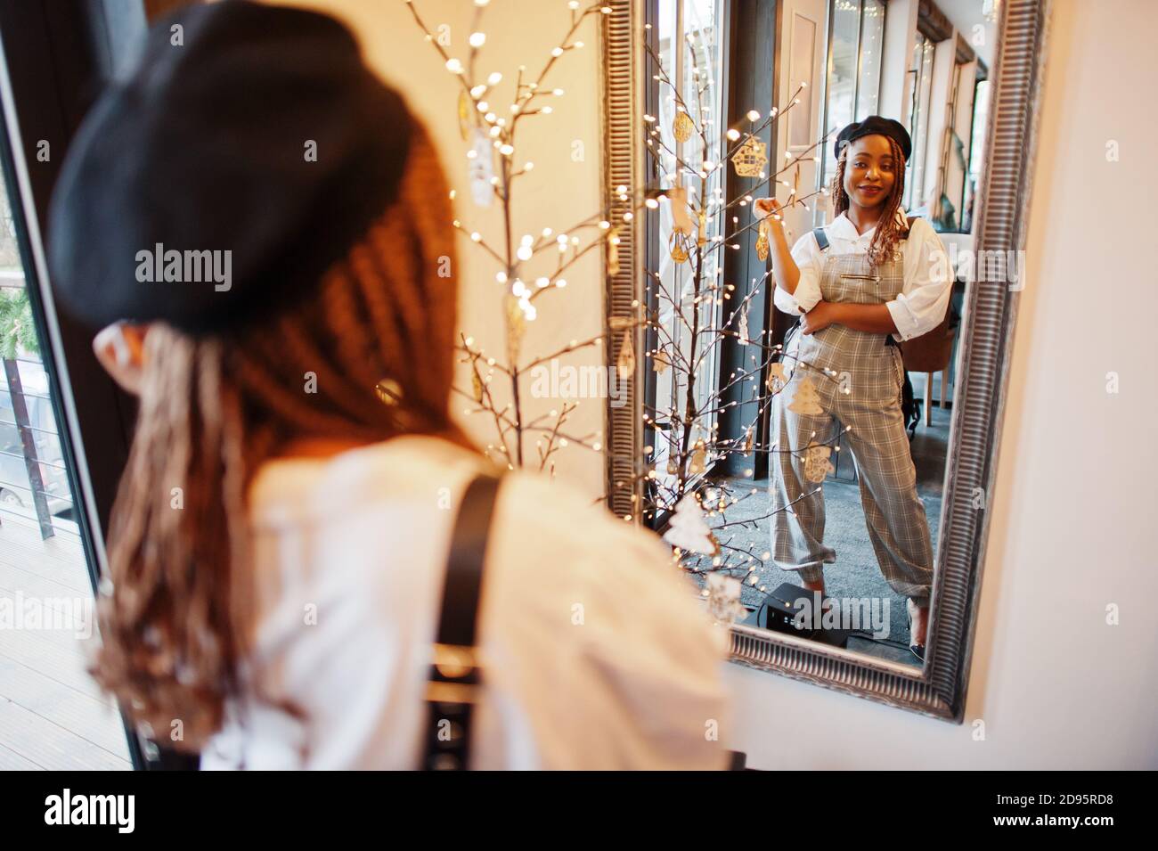 African american woman in overalls and beret against mirror in soft ...