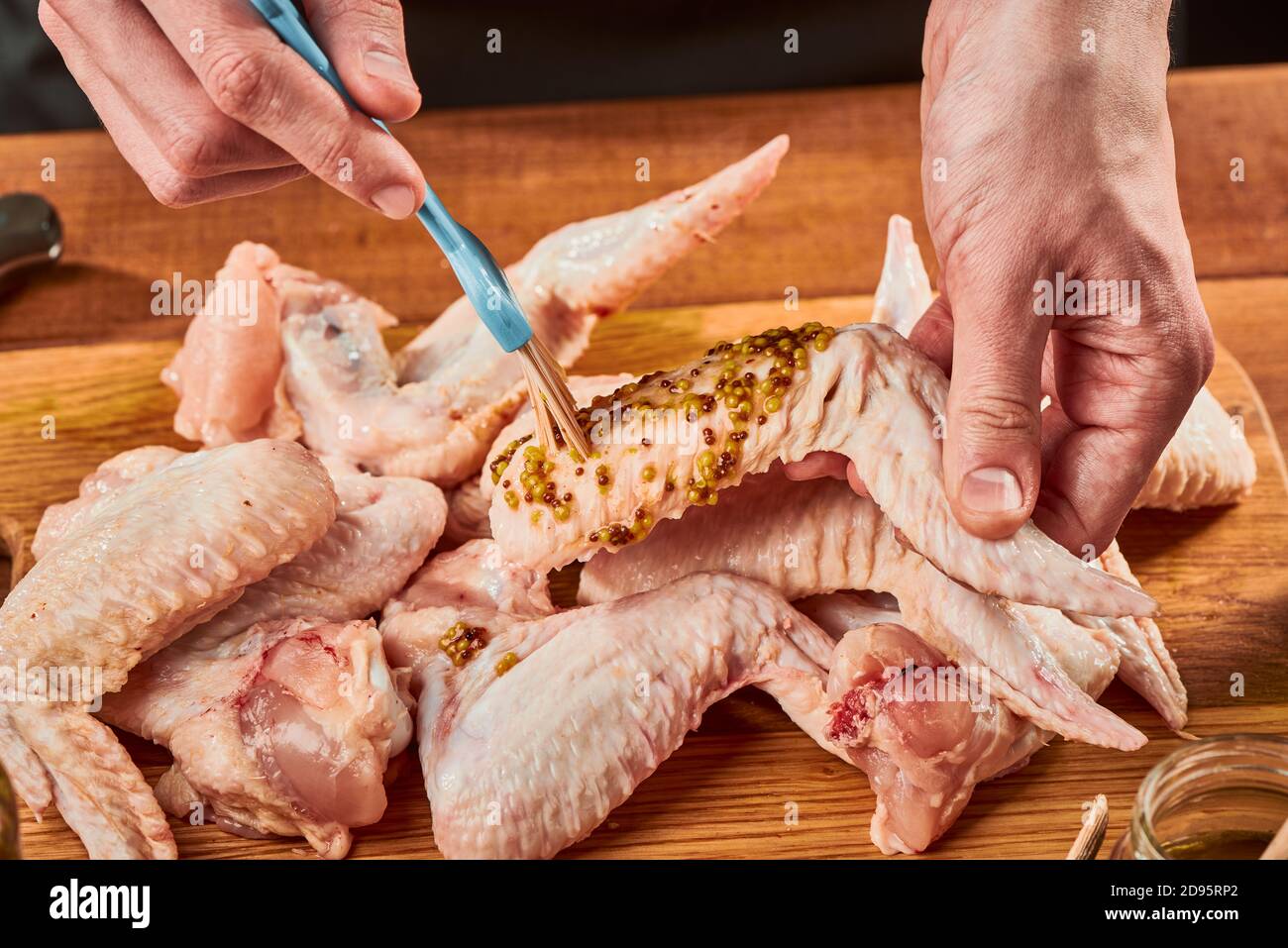 Man brushing raw chicken wings with French mustard Stock Photo - Alamy