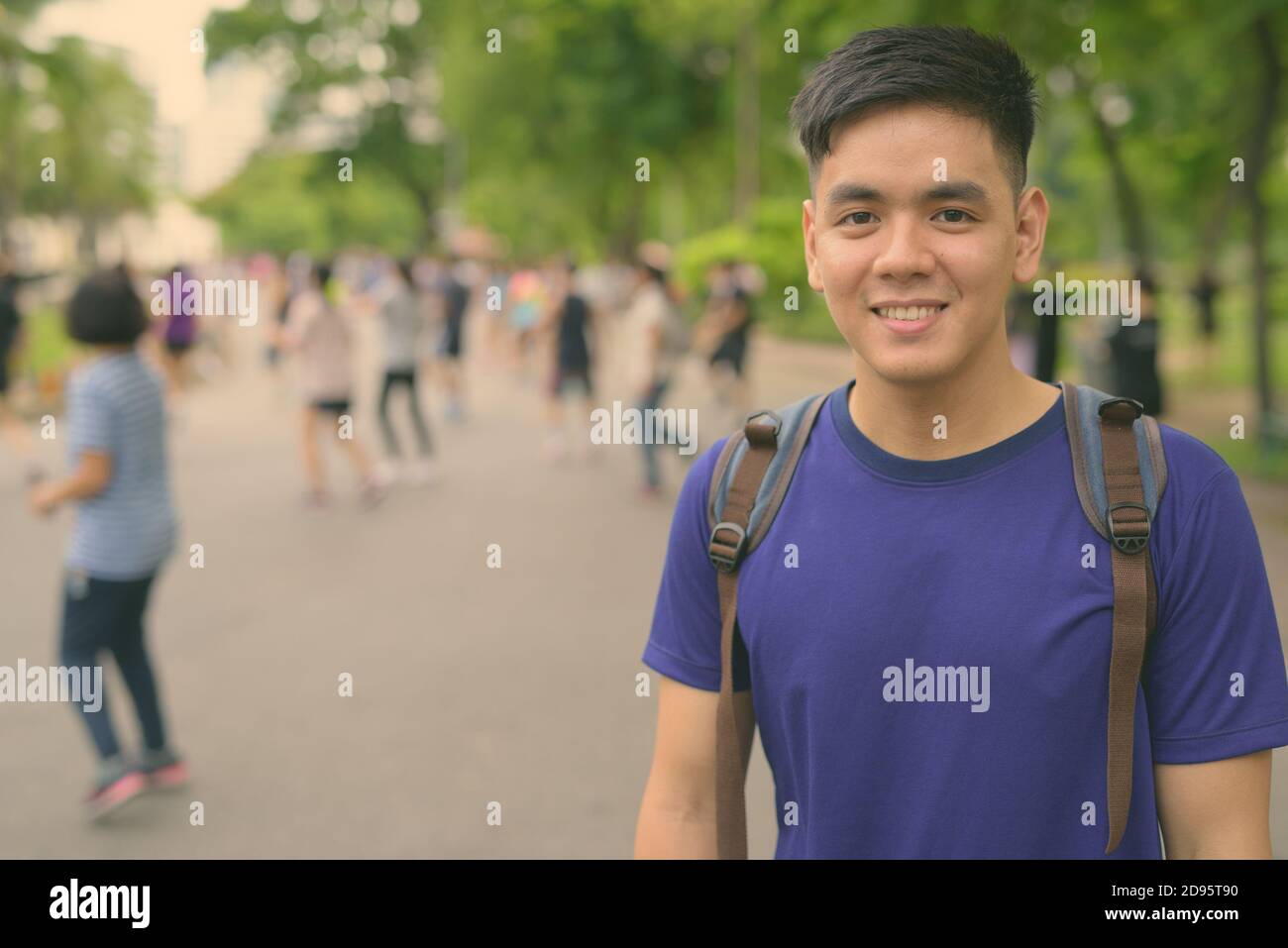 Young handsome Asian tourist man with backpack relaxing at the park ...
