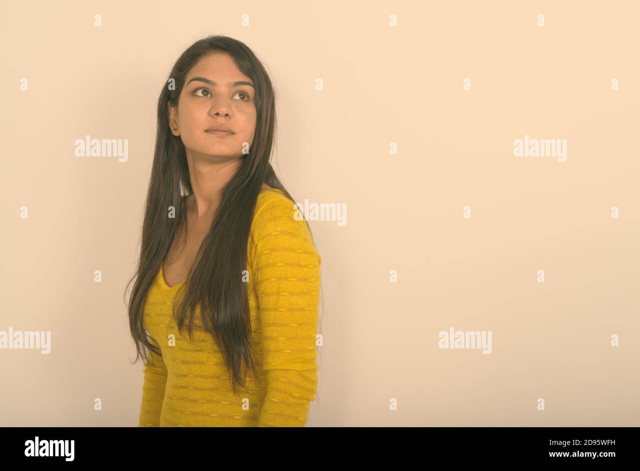 Studio shot of young Indian woman thinking while looking back against ...