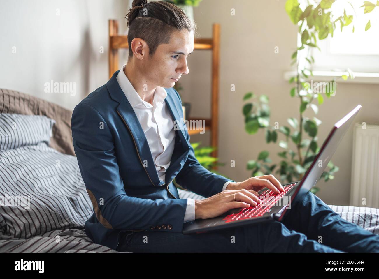 A businessman man in a suit is working remotely on a laptop in bed at ...