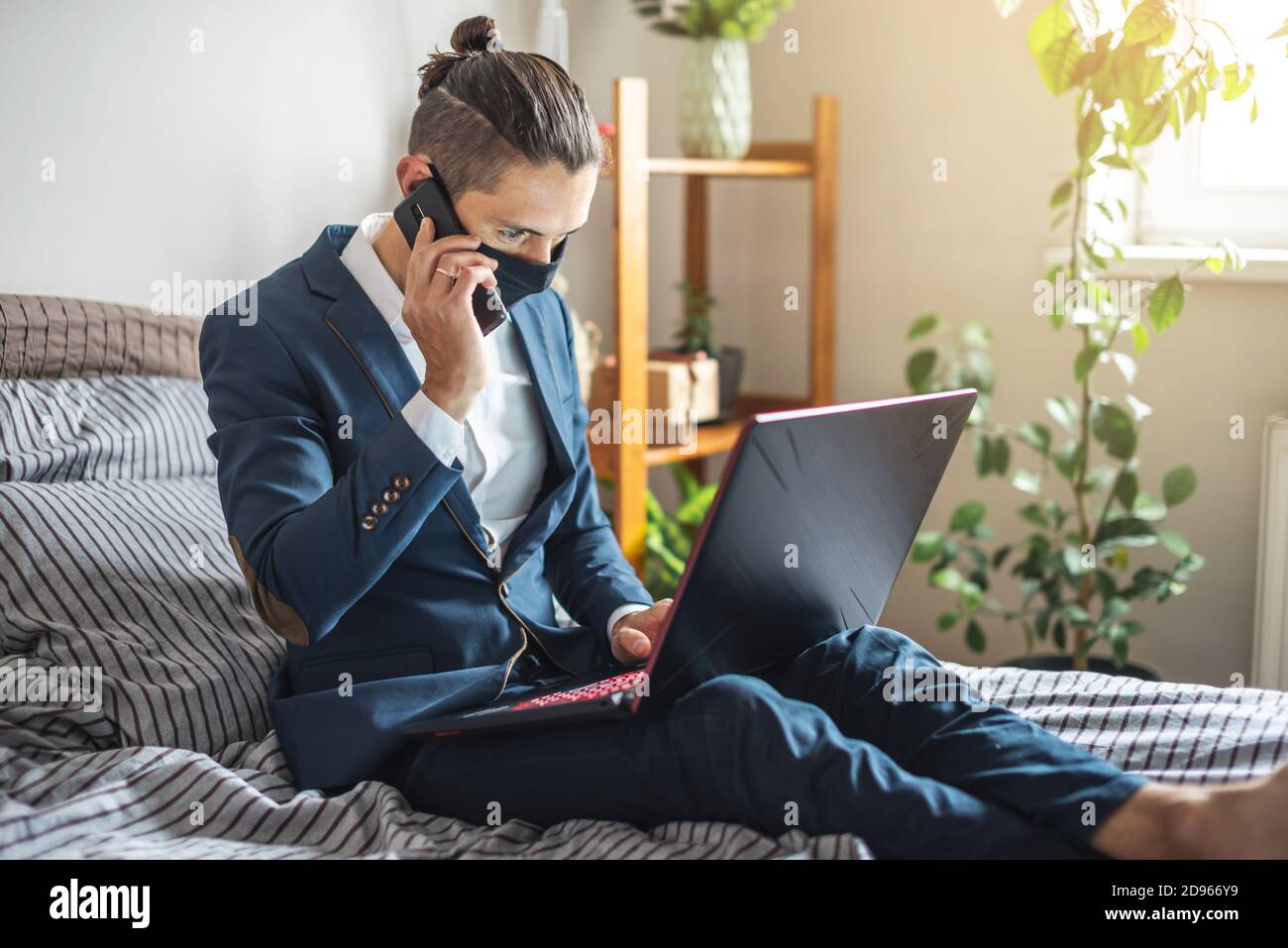 A businessman man in a suit is working remotely on a laptop in bed at ...