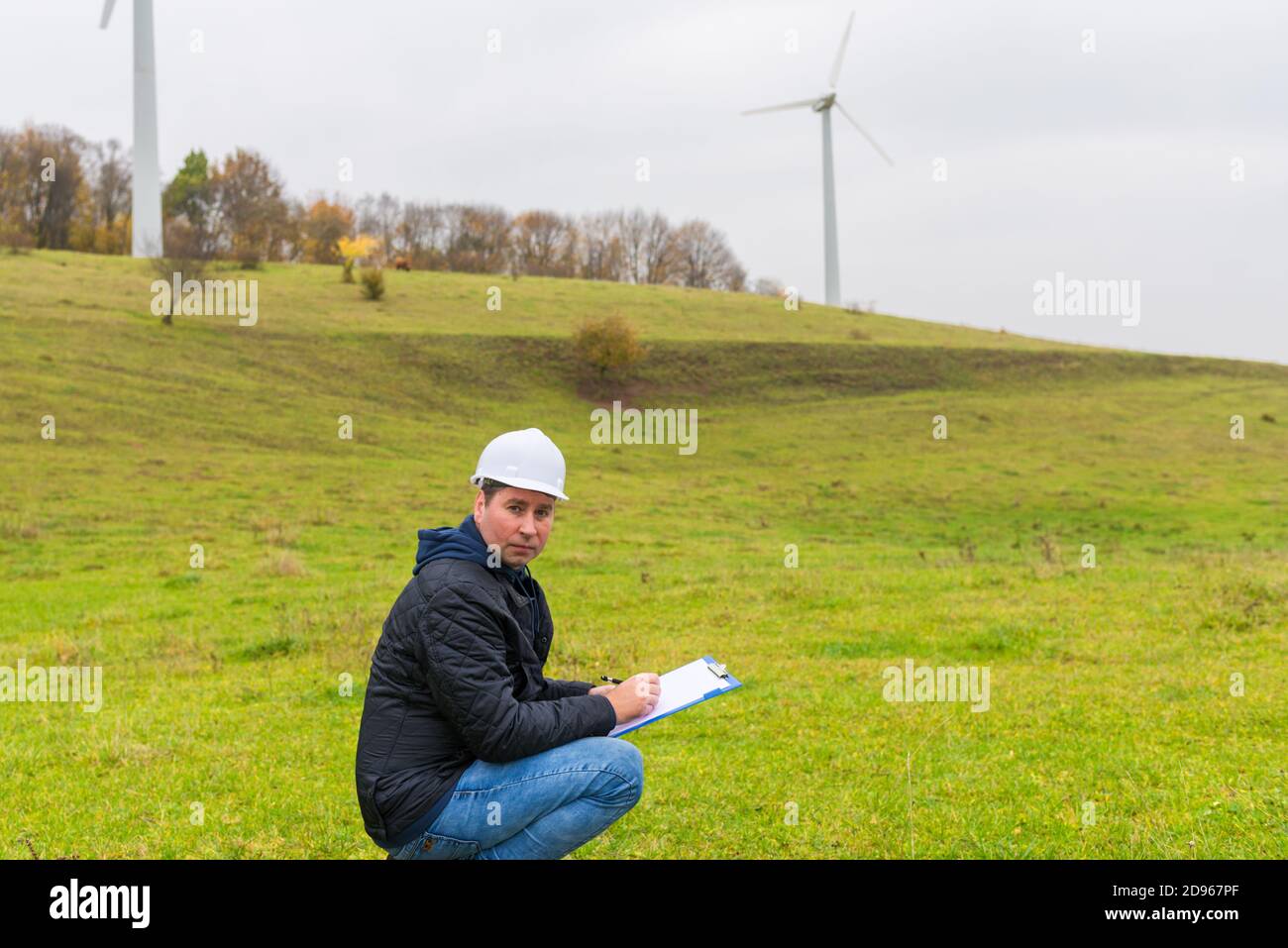 Portrait of squats one male engineer holding a plan at wind turbine at ...