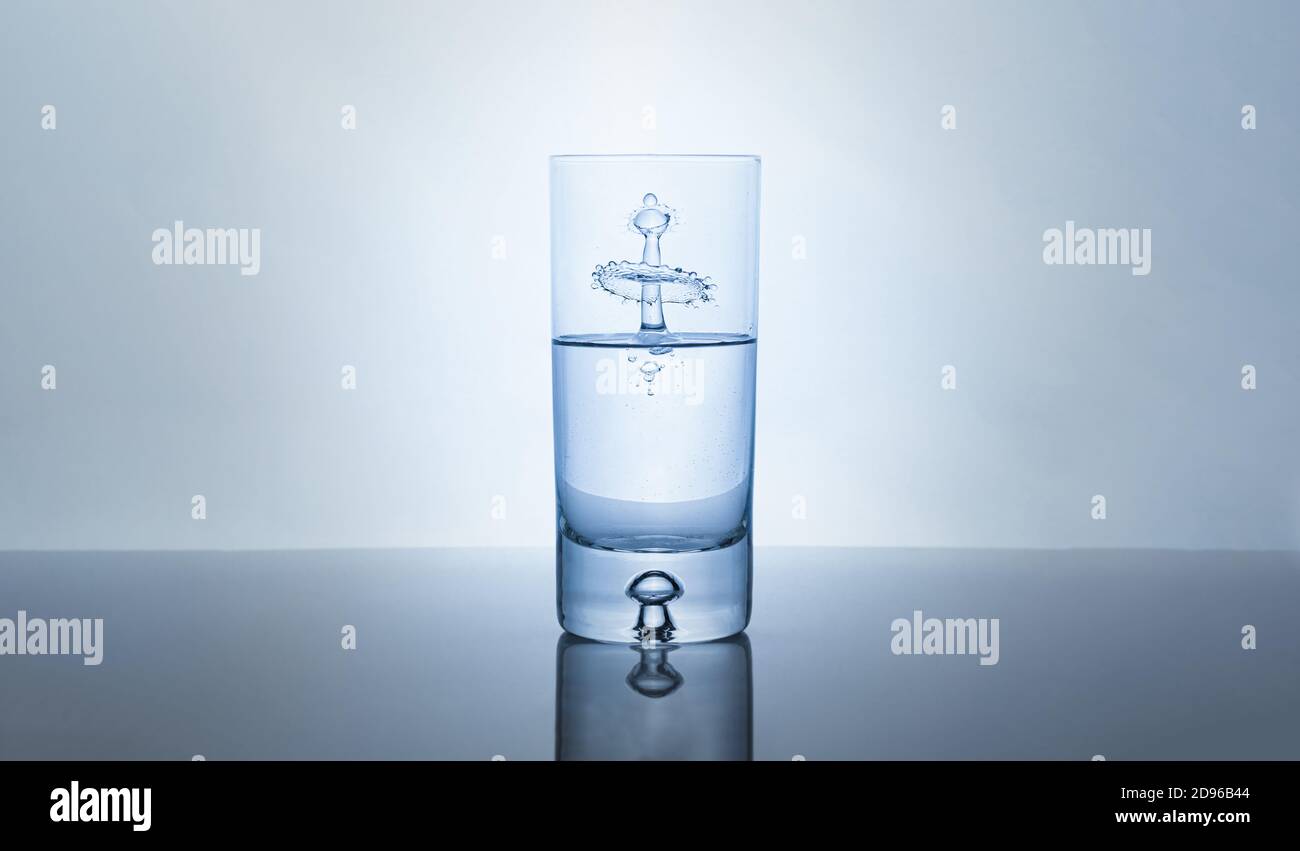Abstract Water drop splash inside glass half full against bright ...