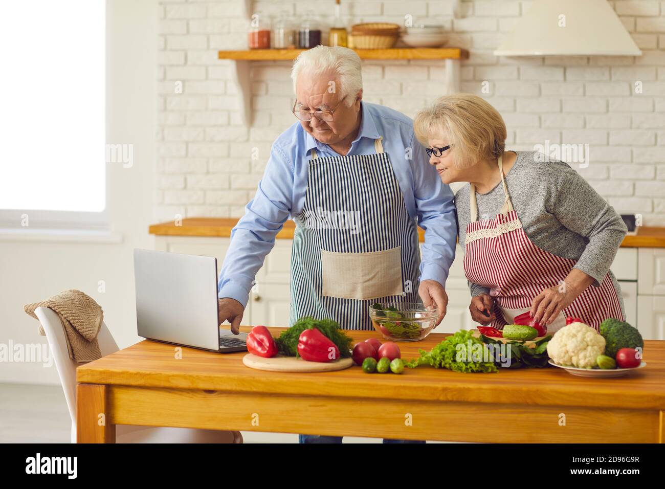 Happy elderly couple cooking healthy vegetarian dinner from online ...