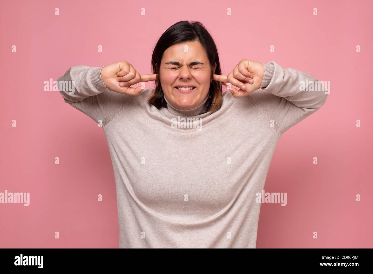Annoyed young woman plugging her ears to avoid loud noise, having ...