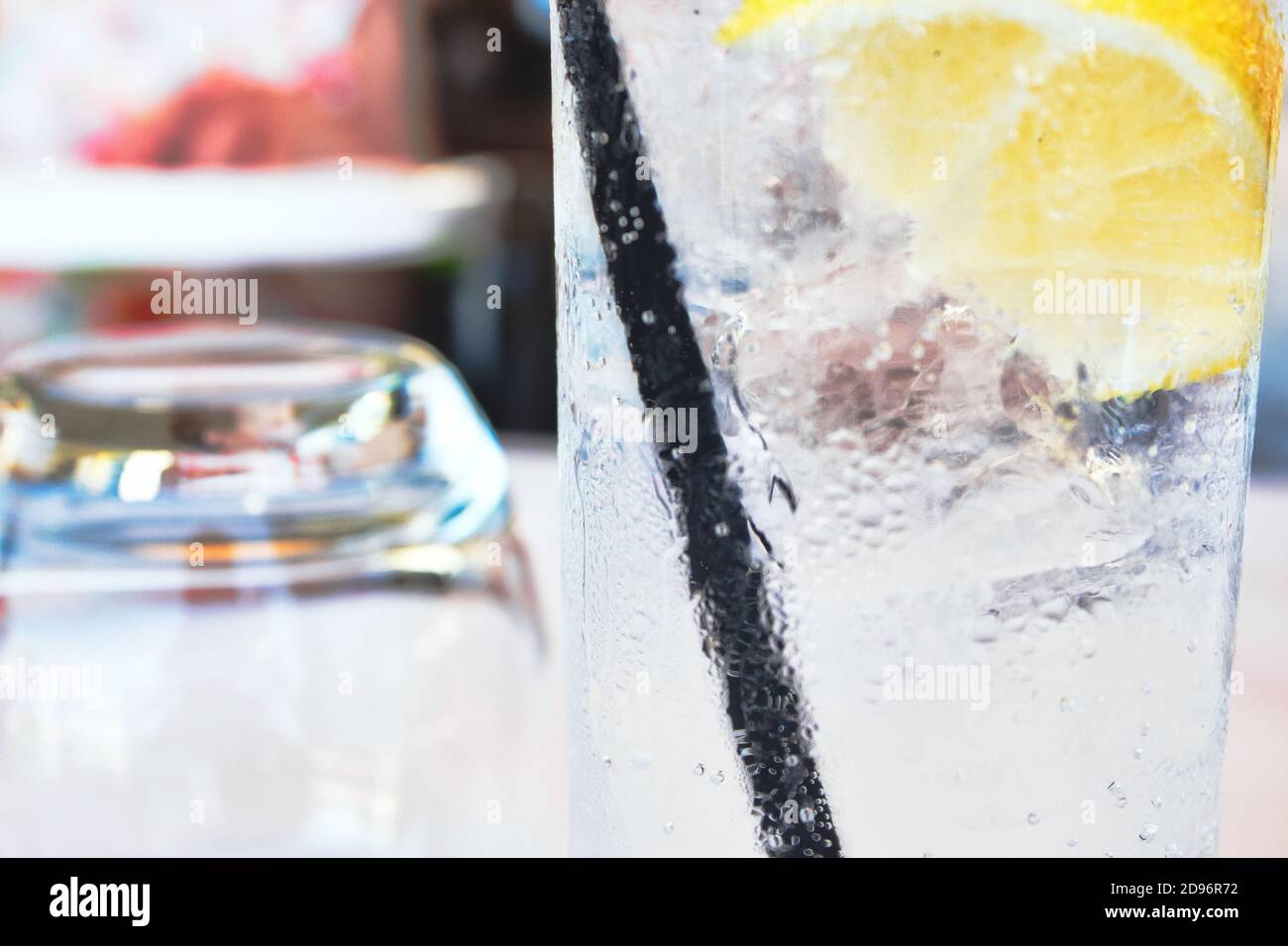 Cold soft drink in a long glass with ice and lemon and a black straw ...