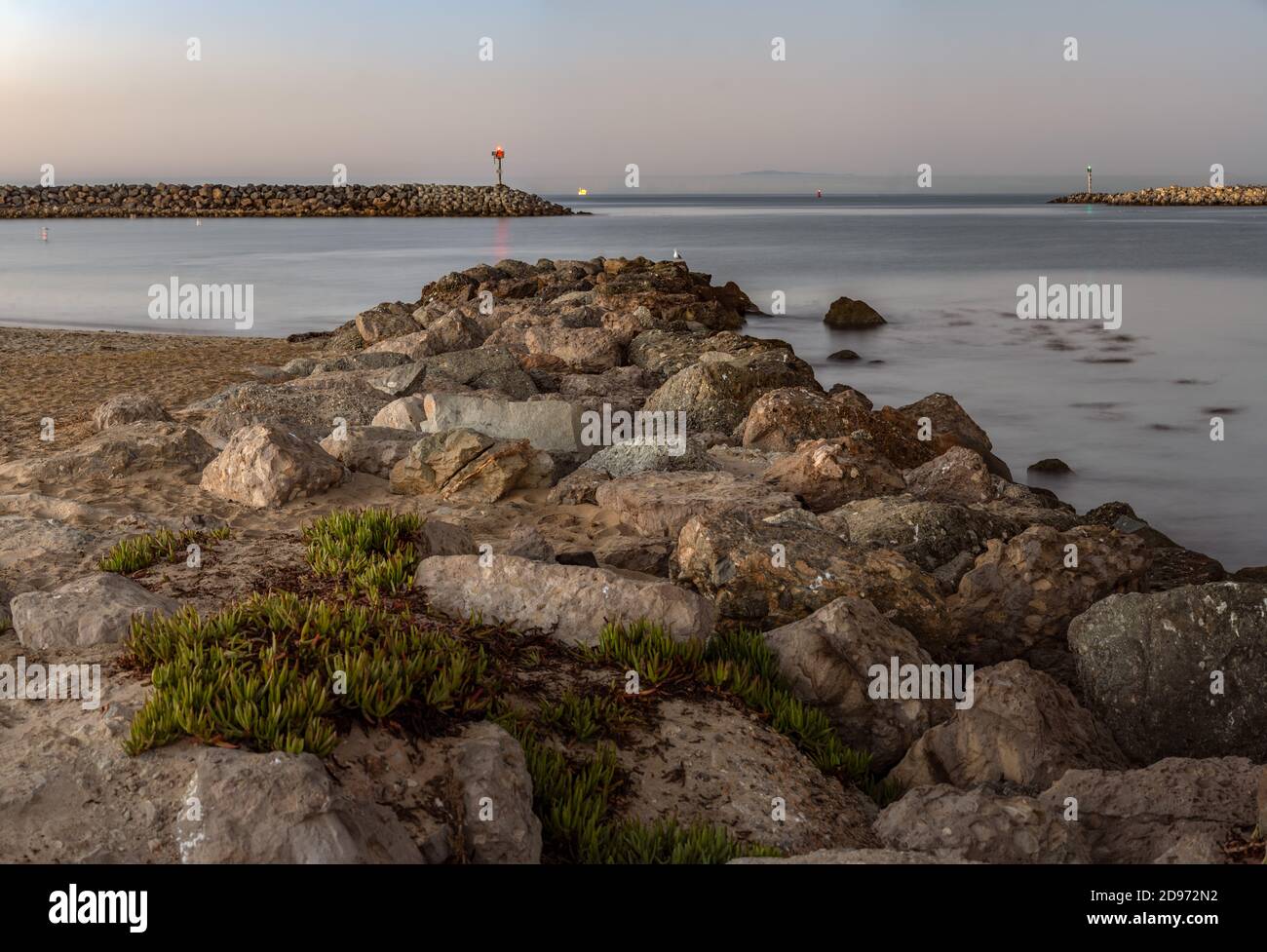 Rock jetty reaches out into the harbor toward fog light at the edge of ...