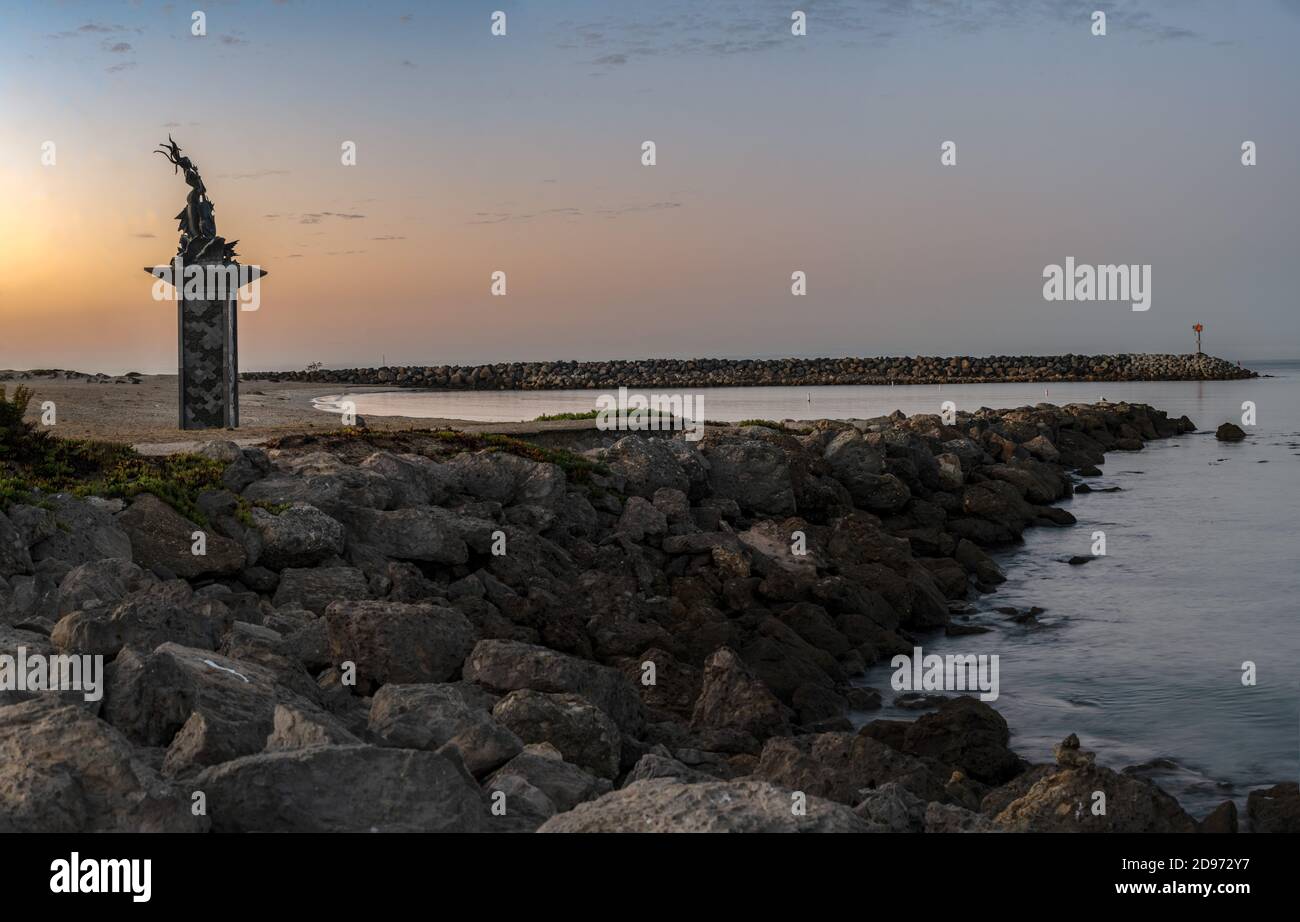 Statue silhouette stands at base of rock jetty just beginning to show ...