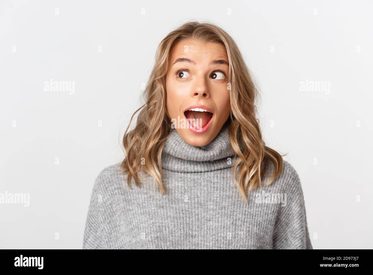 Close-up of amazed blond girl looking at upper left corner, standing ...
