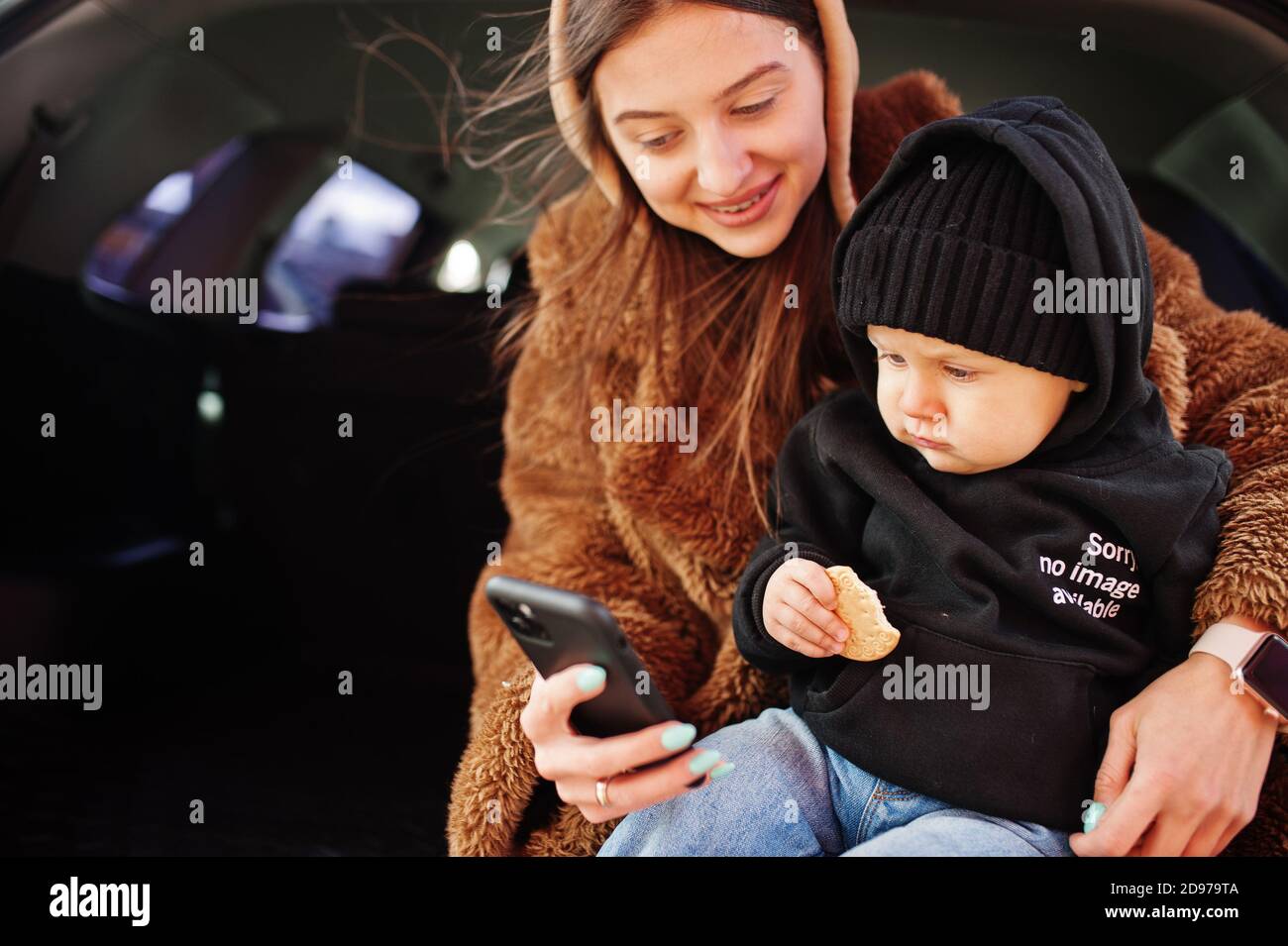 Young mother and child sitting in the trunk of a car and looking at ...