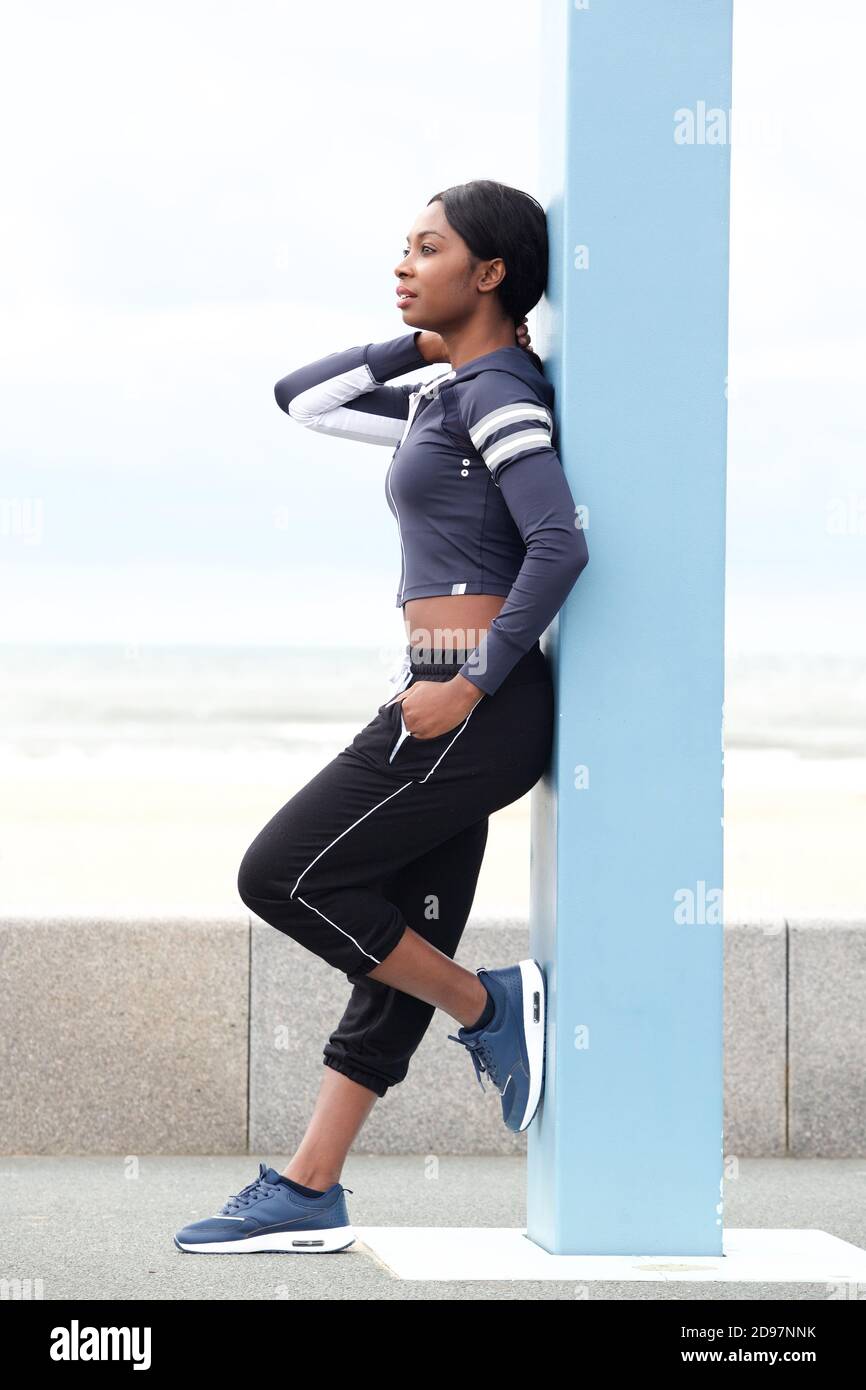 Full length portrait of sporty young black woman leaning against pole ...