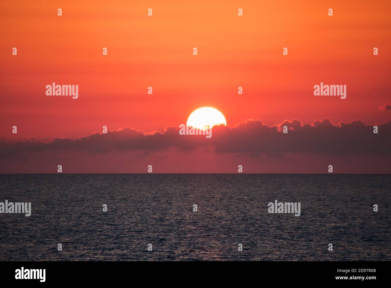 Beautiful sunset with deep red sky and clouds covering the glowing sun ...
