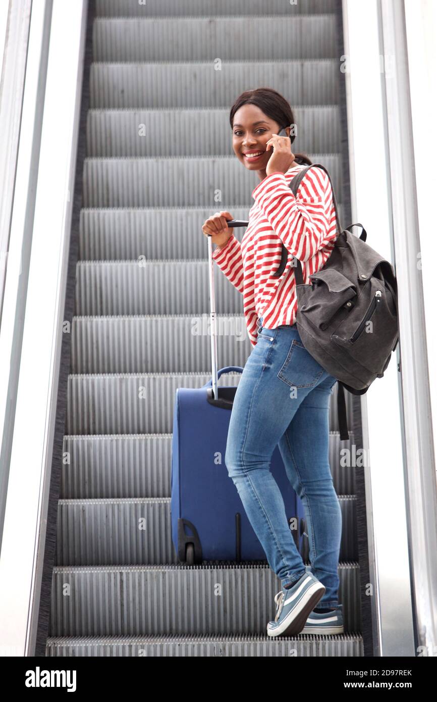Portrait of young black woman on escalator with mobile phone and ...