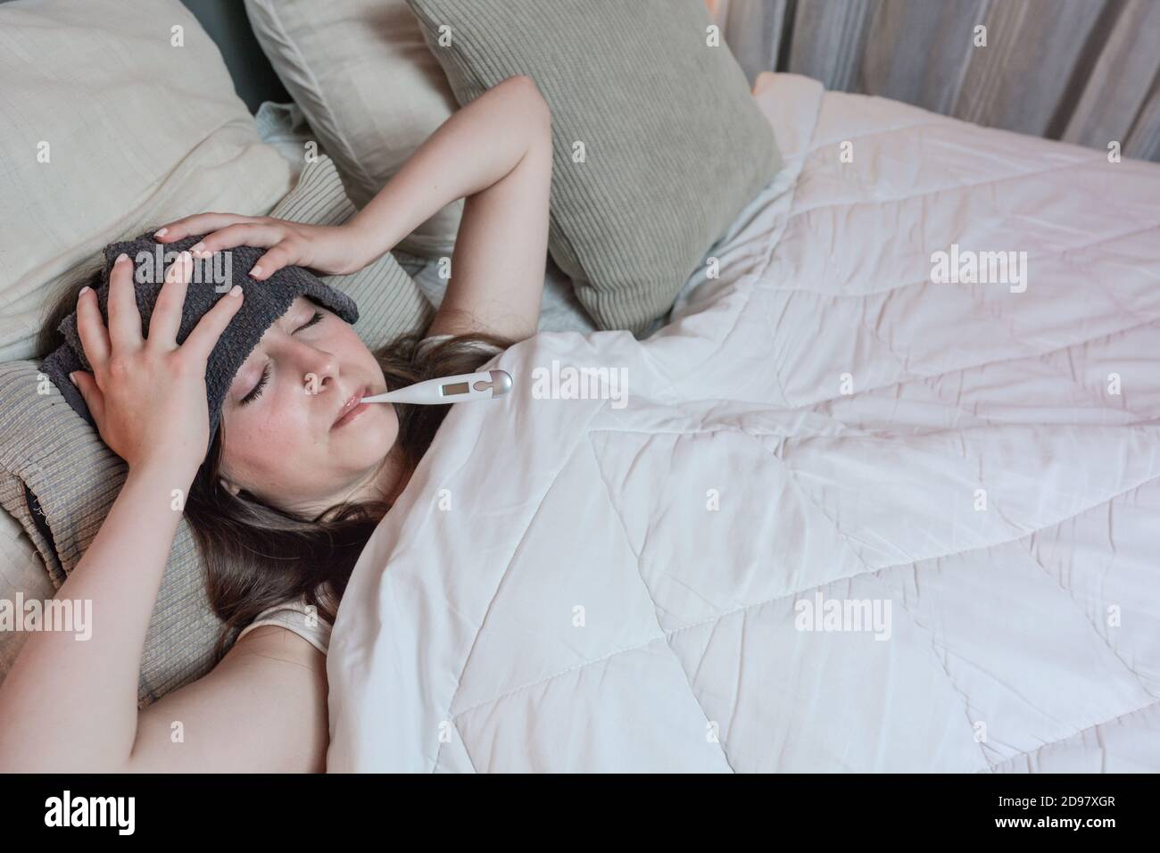 Sick teenage girl with a high fever and a thermometer. She has a cold ...