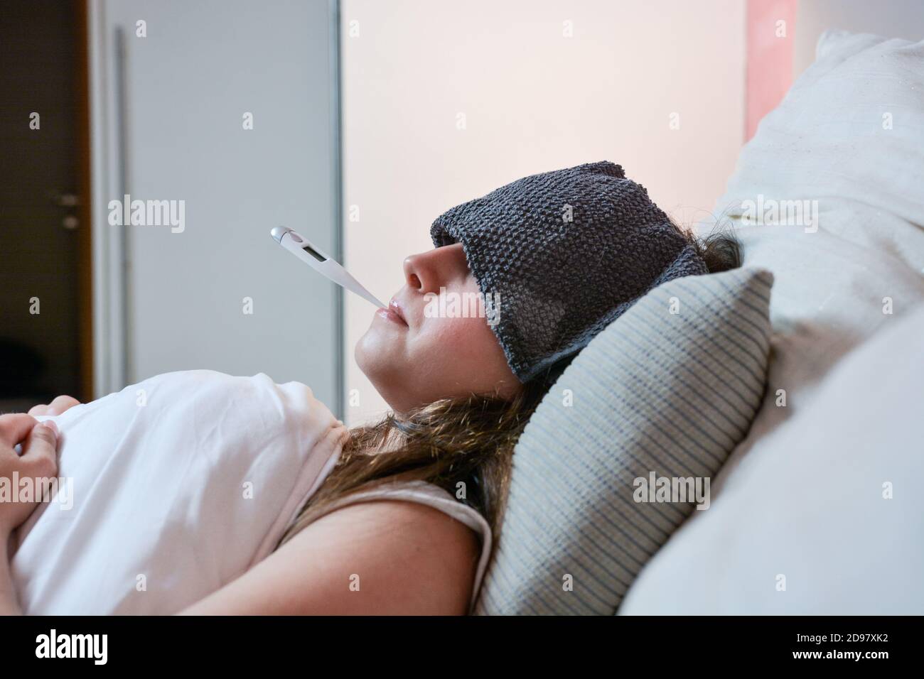 Sick teenage girl with a high fever and a thermometer. She has a cold ...