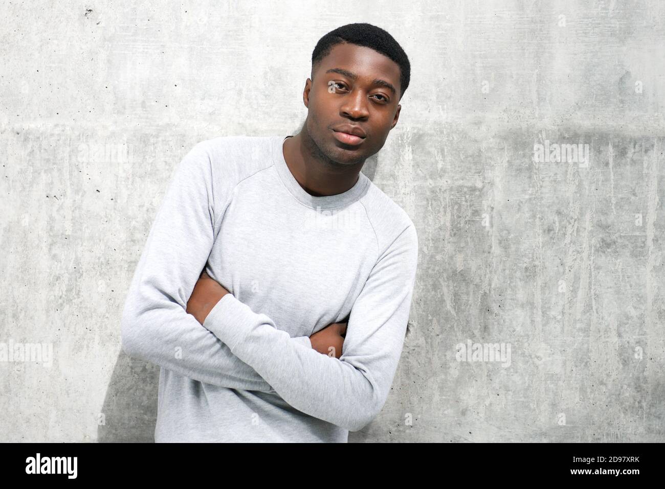Portrait of cool young black man posing with arms crossed against gray ...