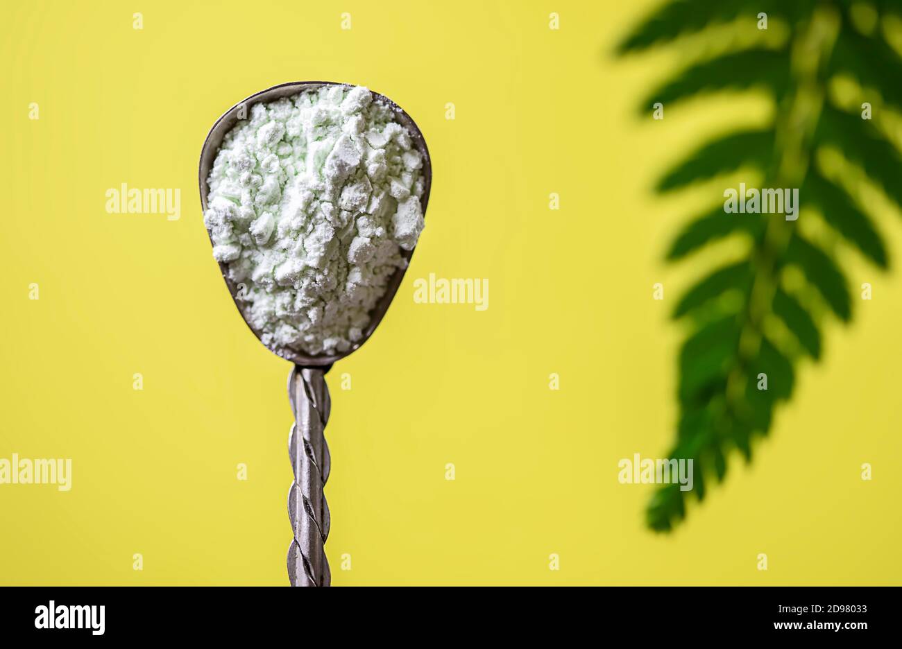 Collagen powder in a spoon and fern leaves on a bright yellow ...