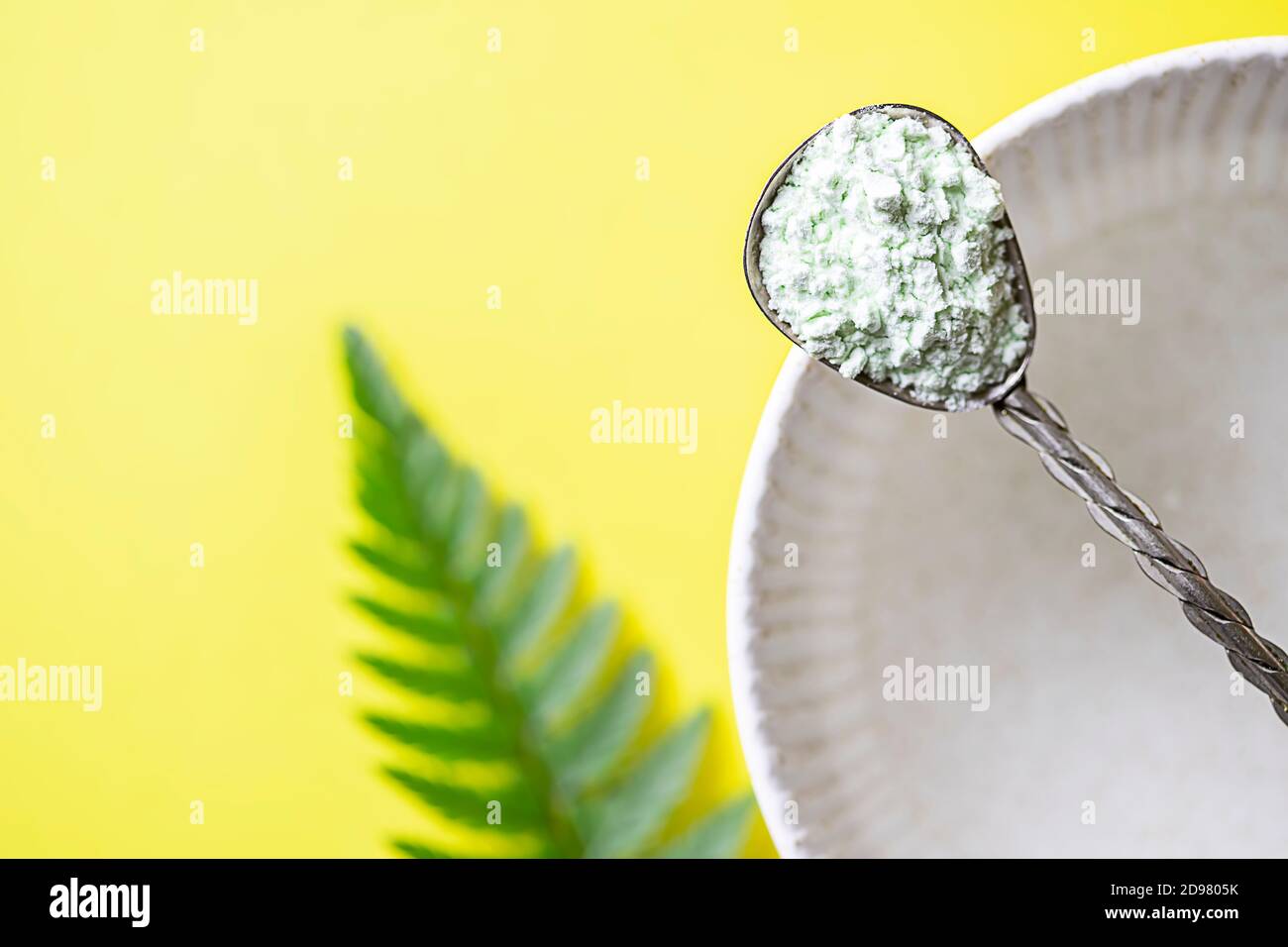 Collagen powder in a spoon and fern leaves on a bright yellow ...