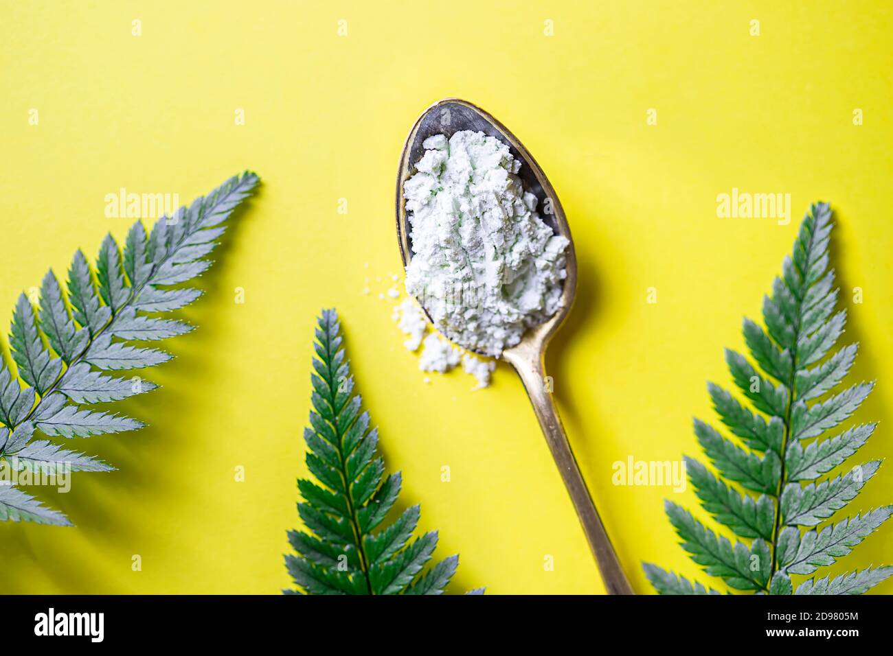 Collagen powder in a spoon and fern leaves on a bright yellow ...