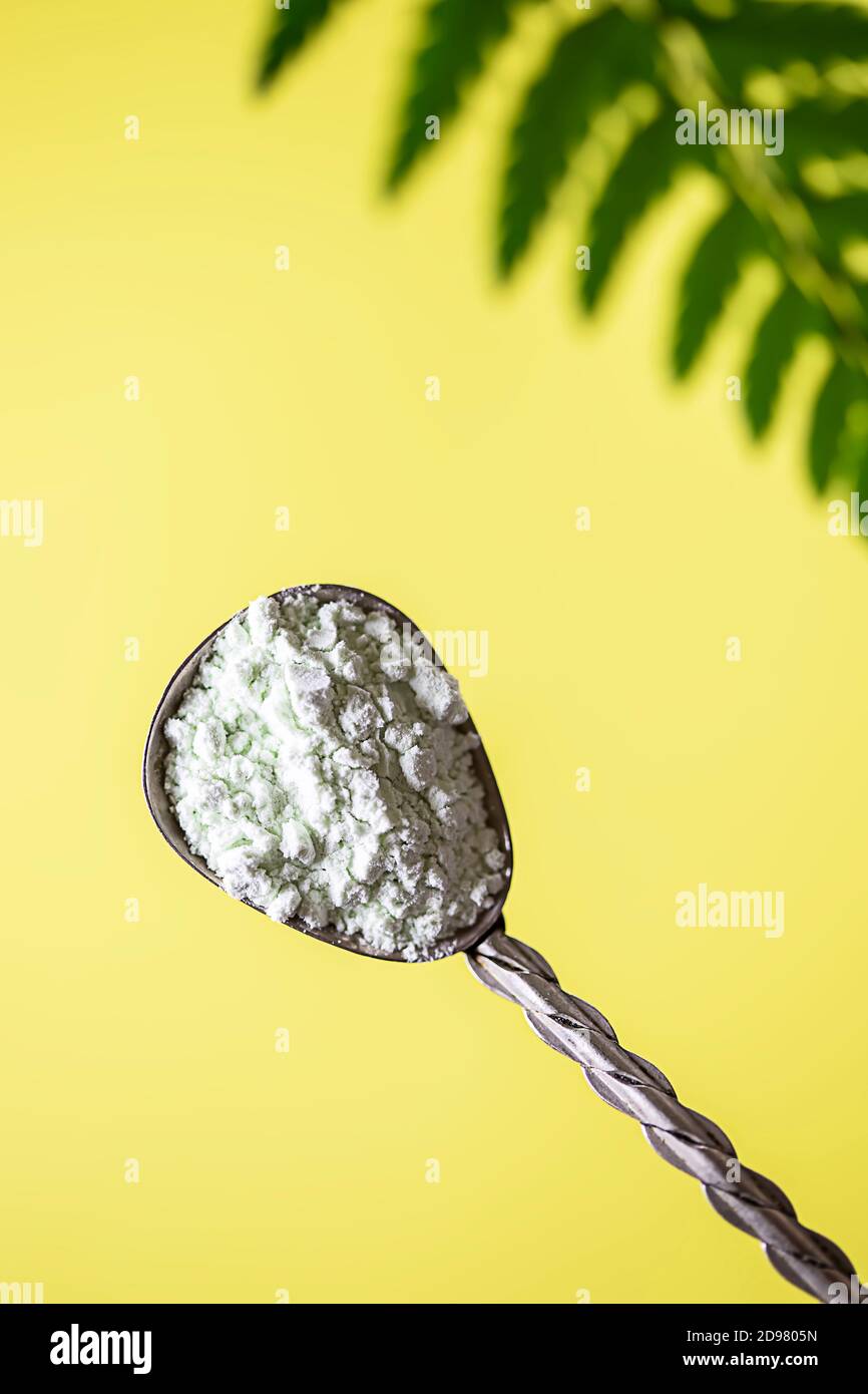 Collagen powder in a spoon and fern leaves on a bright yellow ...