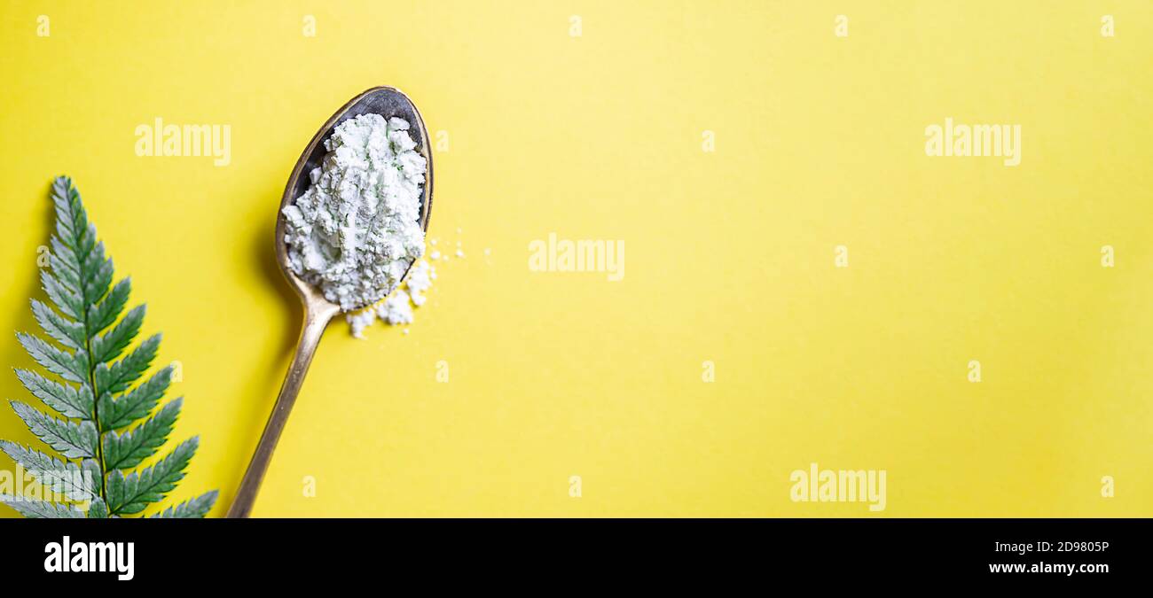 Collagen powder in a spoon and fern leaves on a bright yellow ...