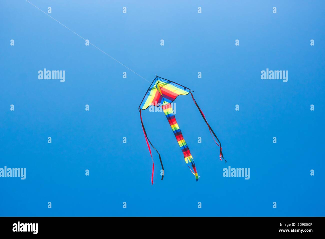 A colourful kite flying in a clear blue sky with a long tail and ...