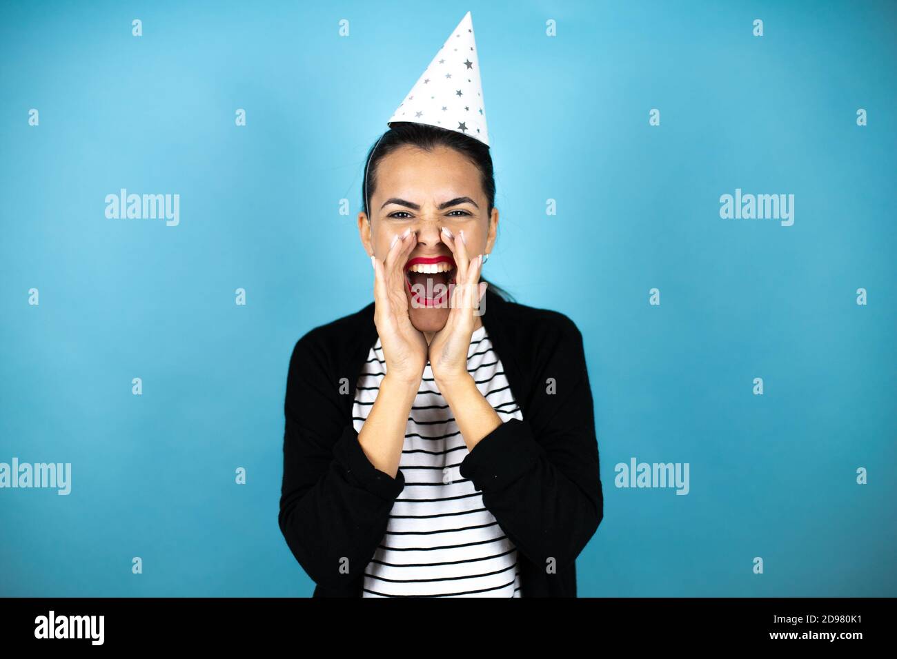 Young beautiful woman wearing a birthday hat over insolated blue ...
