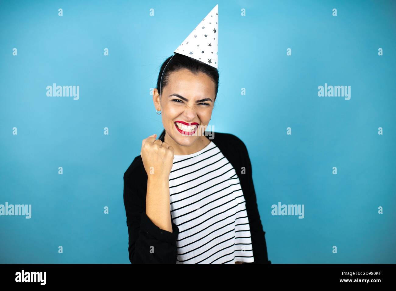 Young beautiful woman wearing a birthday hat over insolated blue ...