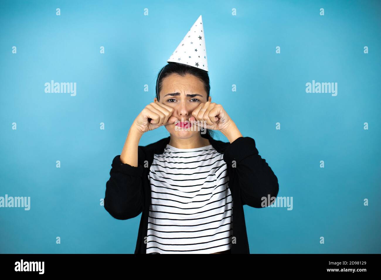 Young beautiful woman wearing a birthday hat over insolated blue ...