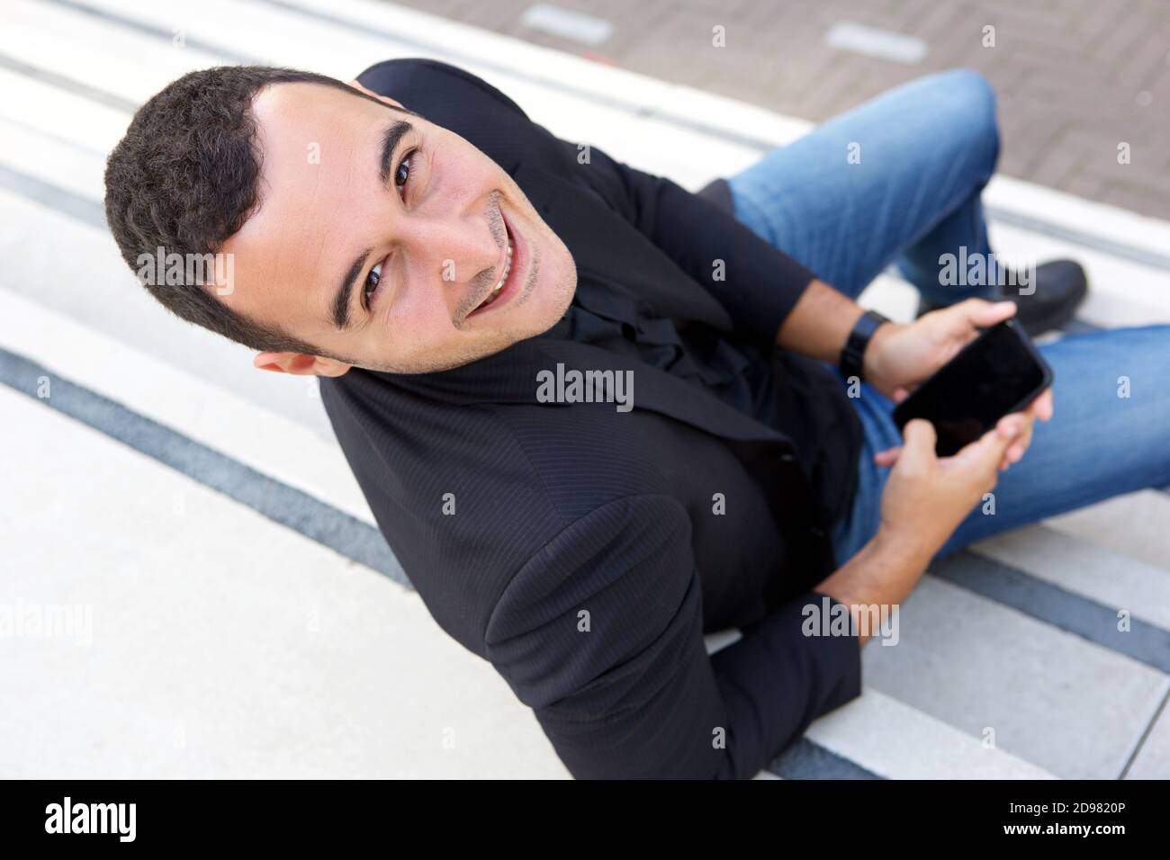 Portrait from above of smiling man sitting on steps and holding ...