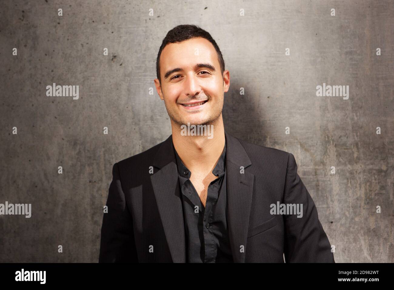 Close up portrait of smiling man posing against gray wall with black ...