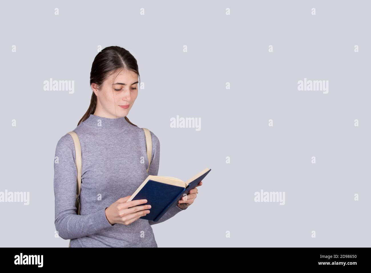 Portrait of contented girl enjoys reading a book, carrying his college ...