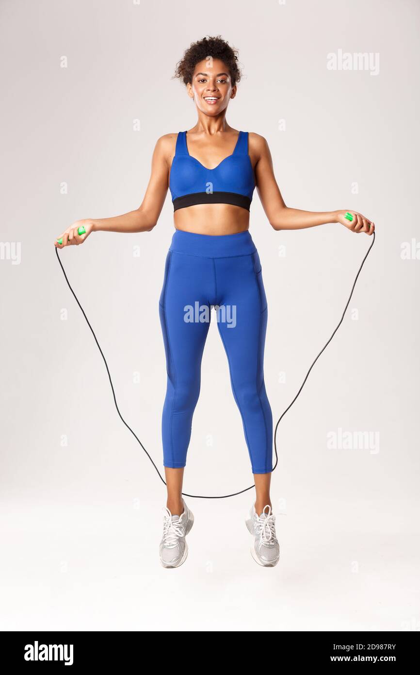 Full length of smiling female athlete in blue sport clothing, jumping ...