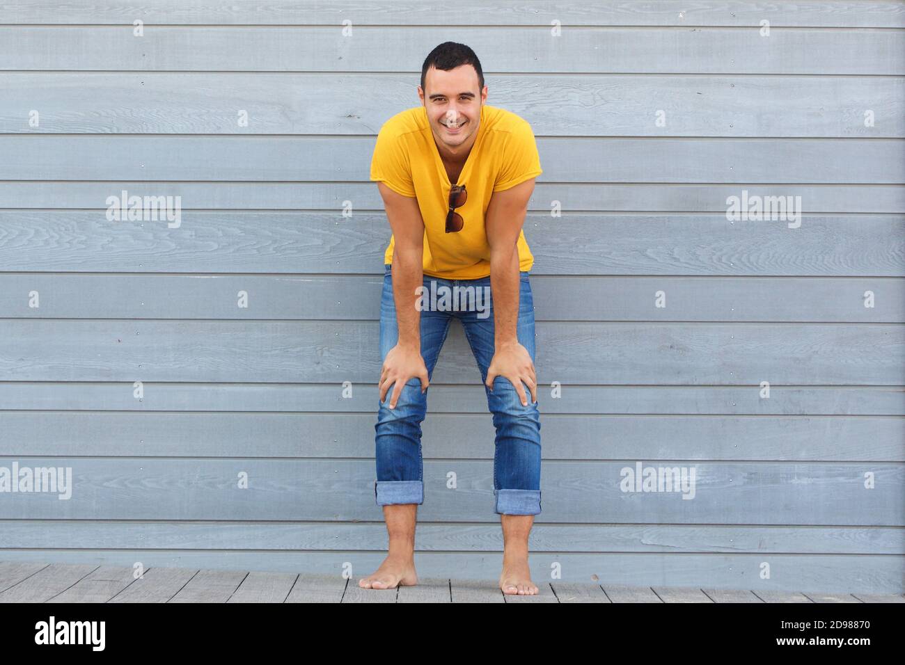 Full body portrait of barefoot man smiling against gray wall with hands ...