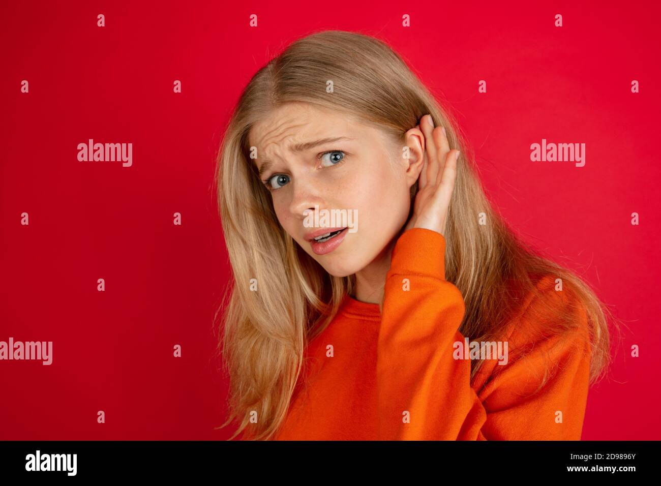 Listening to secret. Portrait of young caucasian woman isolated on red ...
