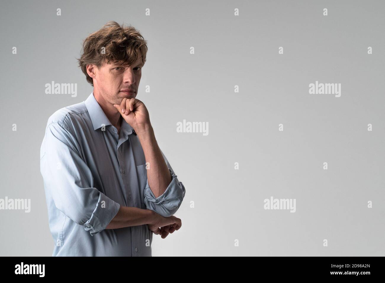 Pensive man looking seriously with fist on his chin against light gray ...