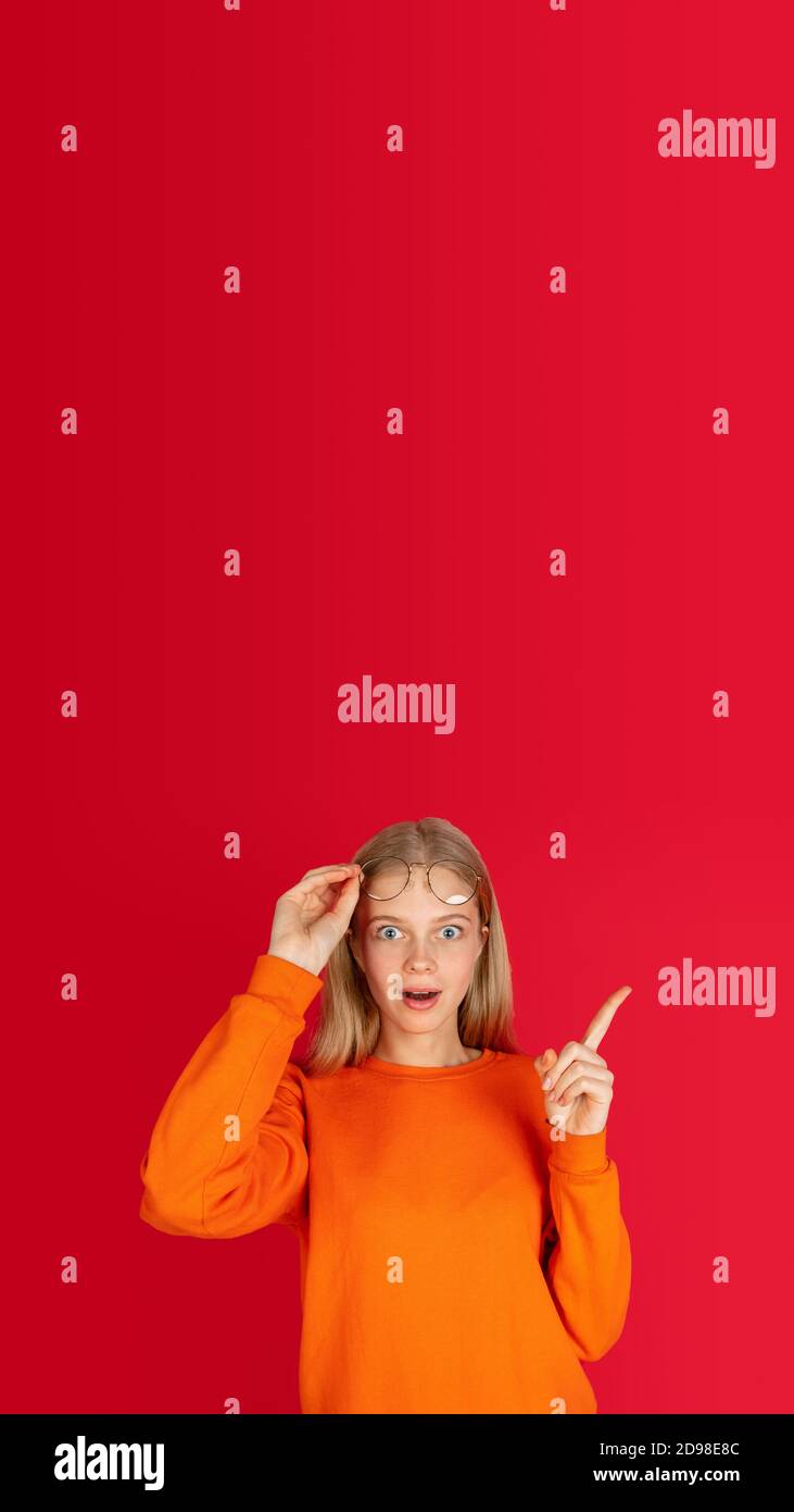 Pointing at side. Portrait of young caucasian woman isolated on red ...