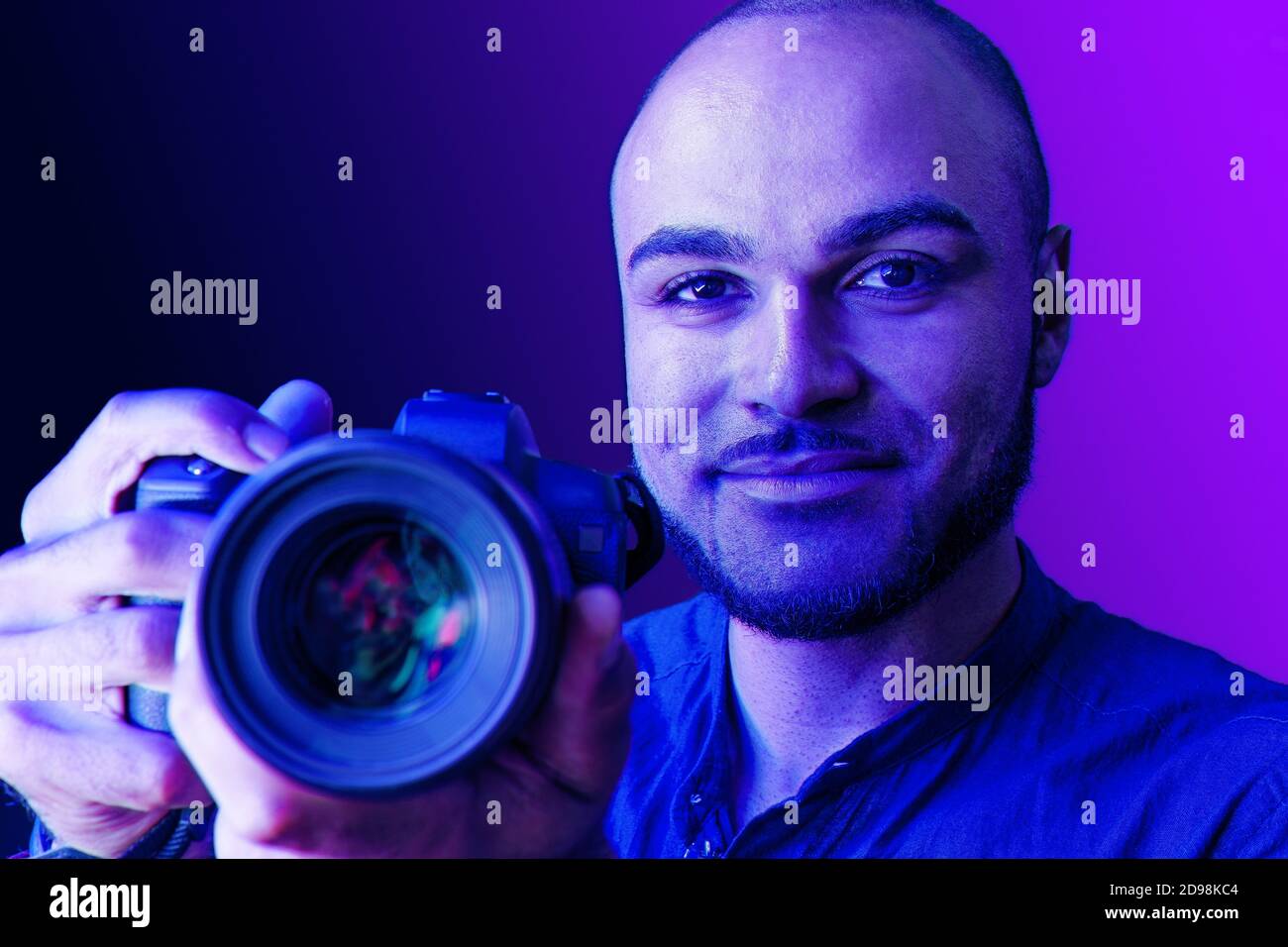 Black man with camera standing against purple background in neon light ...