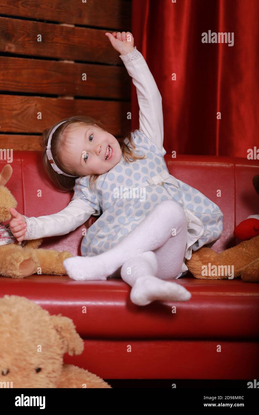 little girl in white polka dots dress having fun on the red couch in ...